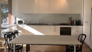 Cozinha moderna com armários brancos, fogão preto e área de refeições com mesa e cadeiras.