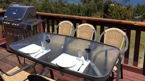 Um terraço com mesa posta para dois, churrasqueira e vista para um lago e montanhas.