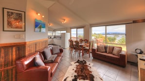 Uma sala de estar ampla com sofá de couro, uma mesa de jantar com cadeiras e uma grande janela com vista para o exterior.