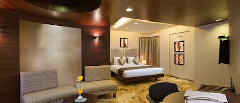Quarto de hotel com cama, sofá, mesa de centro e escrivaninha com um prato de biscoitos.