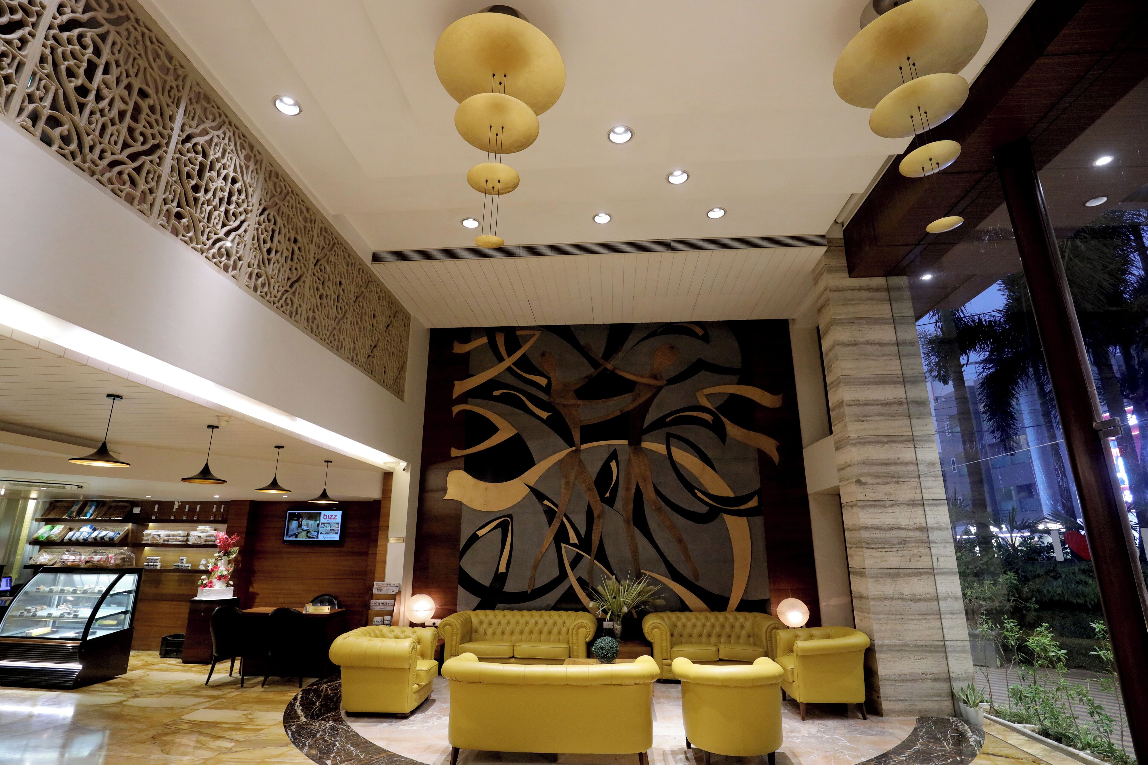 Um lobby com design moderno, apresentando uma grande obra de arte abstrata na parede, uma área de estar com sofás amarelos e uma vitrine com objetos.