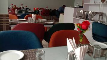 Uma área de refeições com mesas postas, cadeiras em várias cores e um buffet ao fundo.