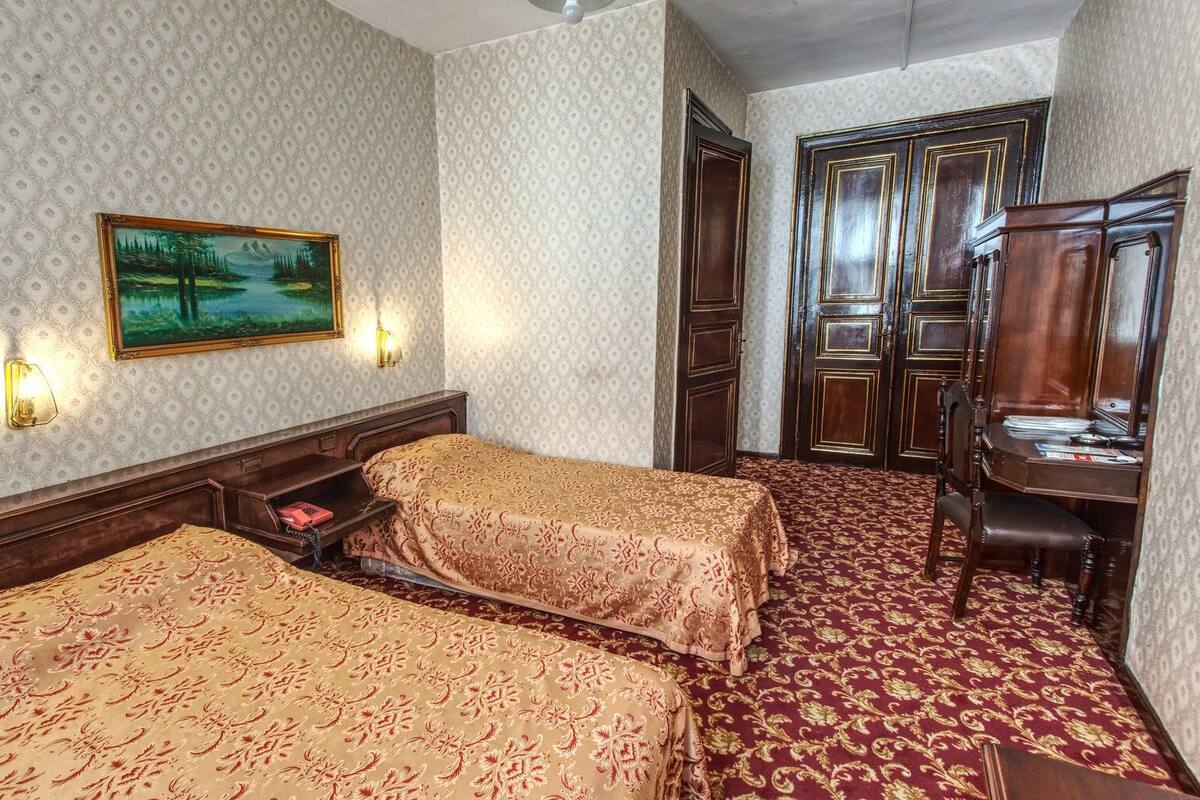 Quarto de hotel com duas camas, uma escrivaninha, uma cadeira, um guarda-roupa e um quadro na parede.