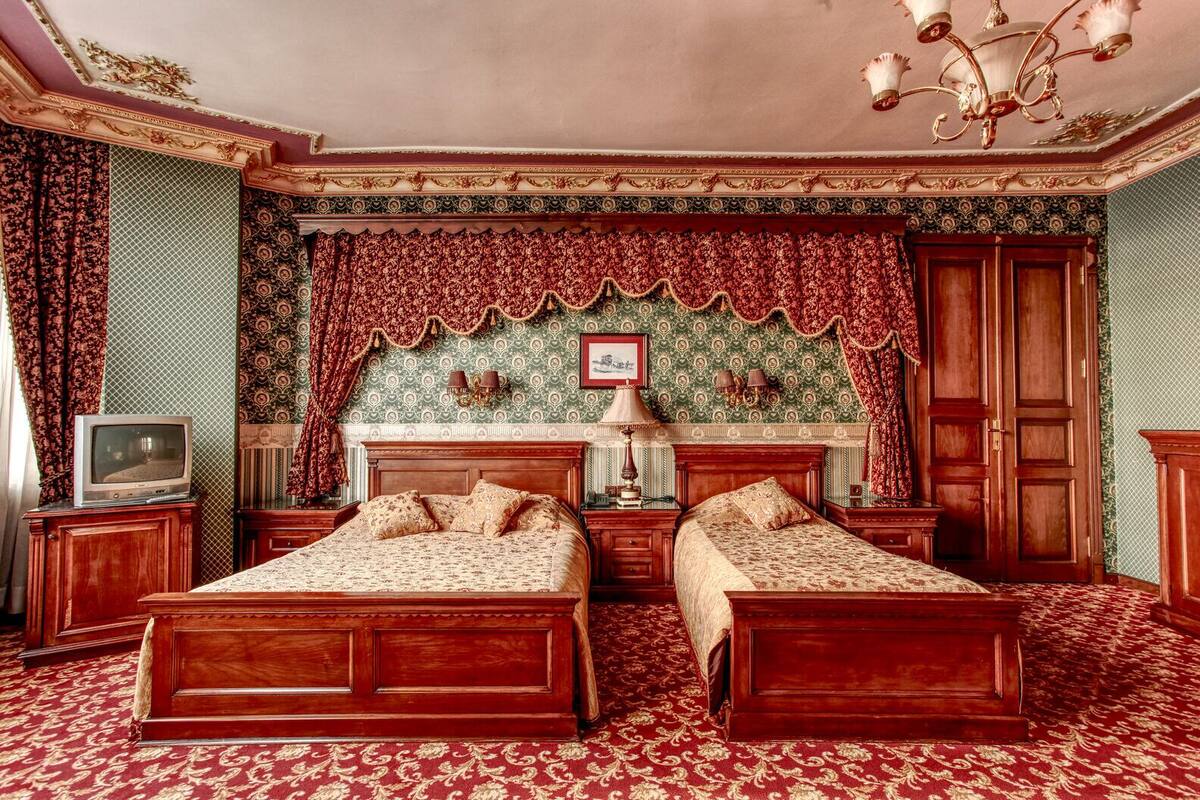 Quarto tradicional com duas camas de madeira, um candelabro e papel de parede estampado.