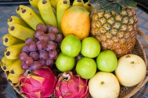 Uma cesta com diversas frutas, incluindo bananas, uvas, maçãs, pitaya, manga e abacaxi.