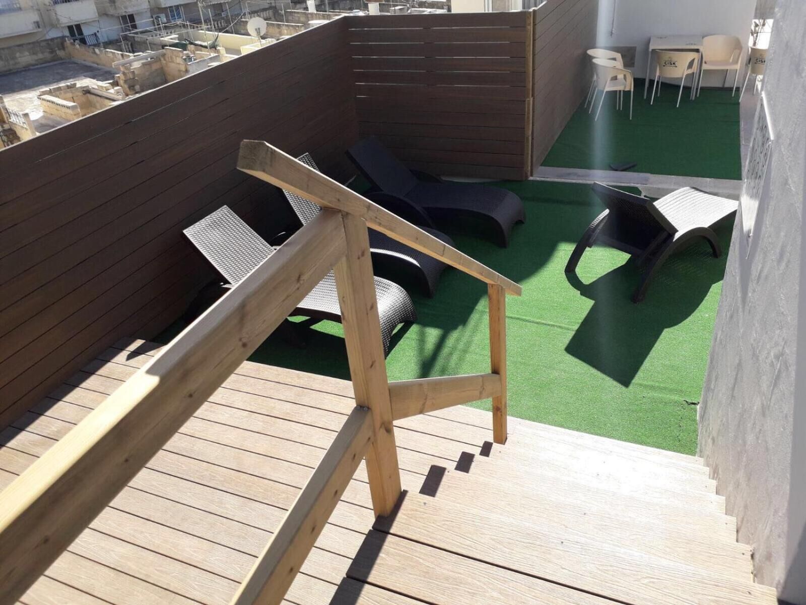 Um terraço no telhado com piso de madeira, guarda-corpo de madeira e mobiliário de exterior, incluindo cadeiras e uma mesa.