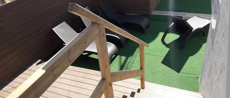 Um terraço no telhado com piso de madeira, guarda-corpo de madeira e mobiliário de exterior, incluindo cadeiras e uma mesa.
