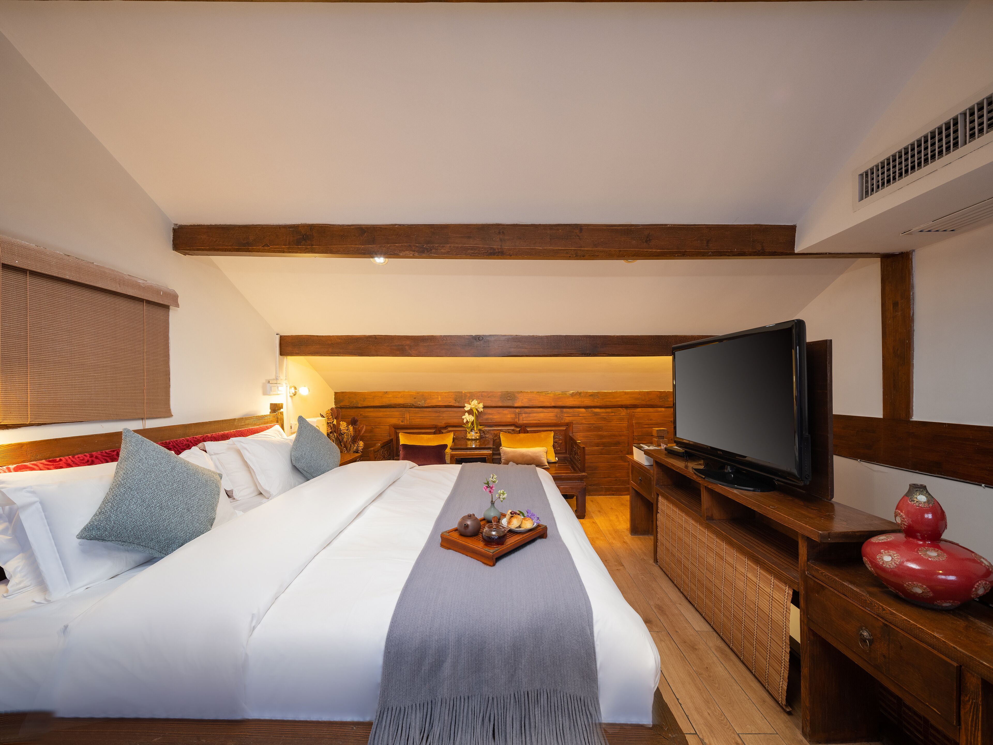 Quarto de hotel com uma cama grande, uma televisão e um painel de cabeceira em madeira.