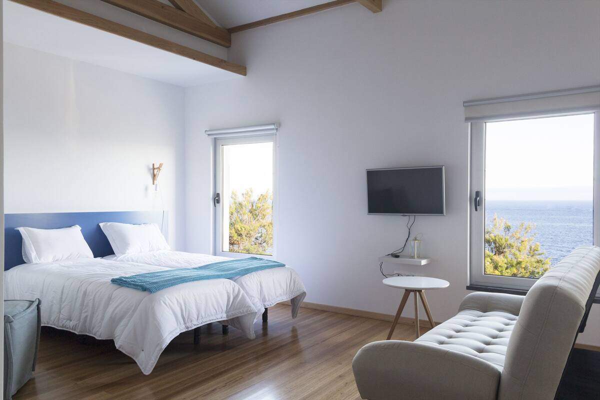 Quarto com cama, televisão, janela com vista e sofá.