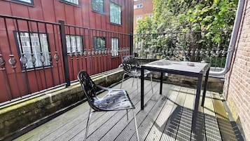 Um pátio externo com mesa e cadeiras, um edifício vermelho com janelas e uma cerca de metal.