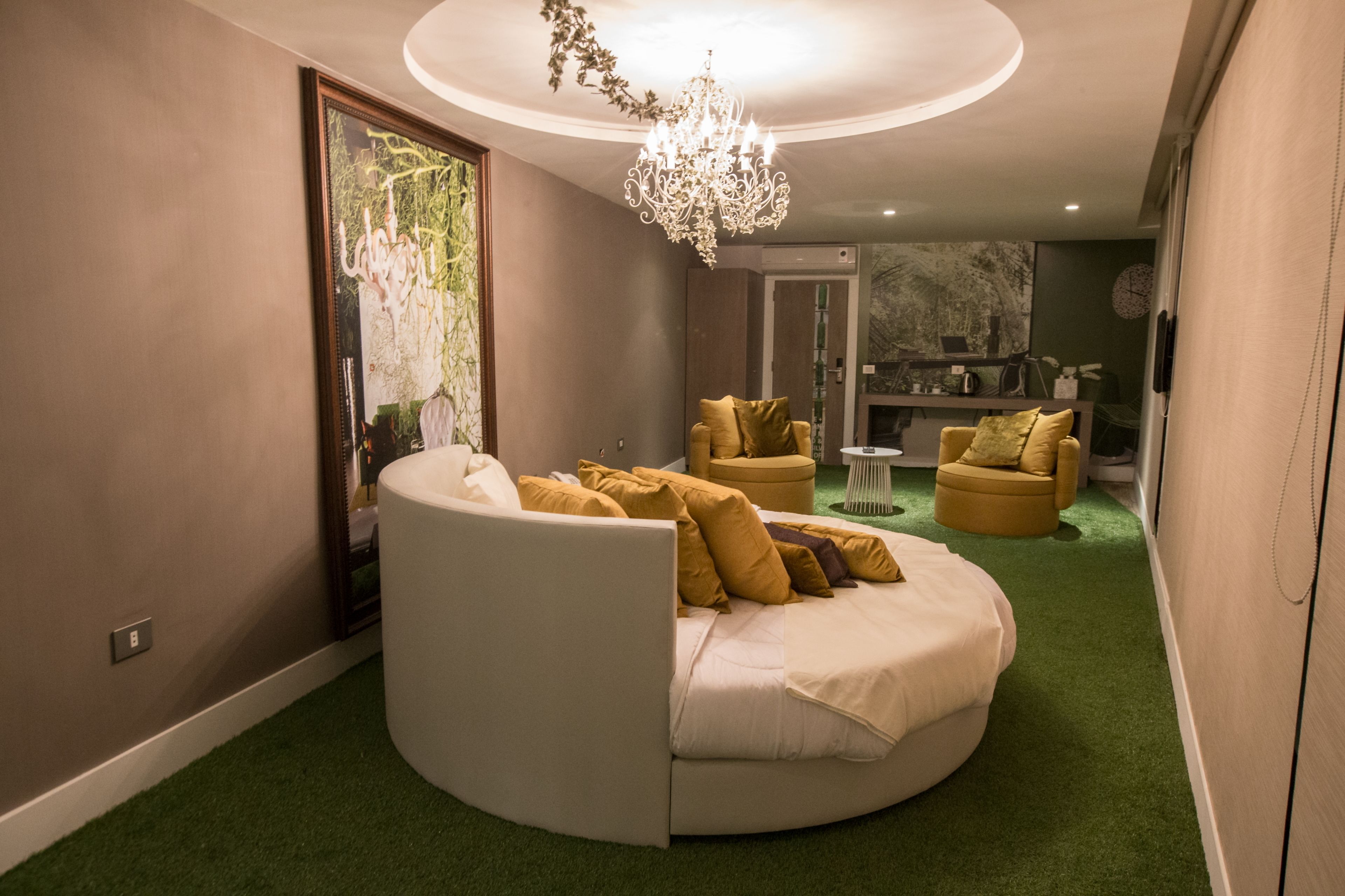 Uma área de estar circular com um sofá branco e almofadas amarelas, um candelabro e um tapete verde.