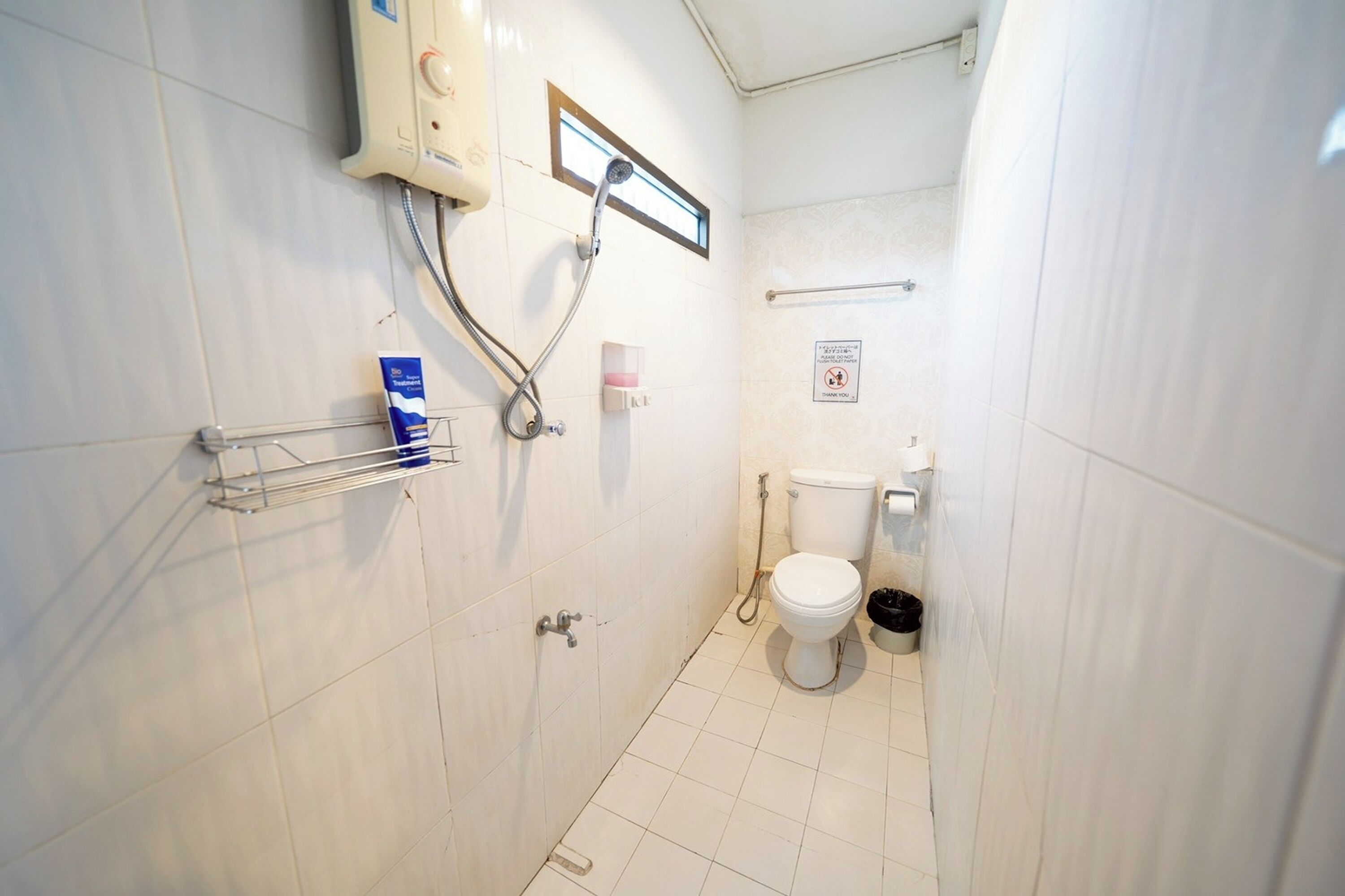 Um banheiro pequeno e limpo com azulejos brancos, vaso sanitário, bidê, porta-toalhas e chuveiro.