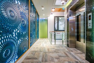 Um elevador moderno com visor digital, painel de madeira e parede verde.