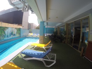 Área da piscina com espreguiçadeiras, um mural e uma porta de vidro que dá para um espaço interno.