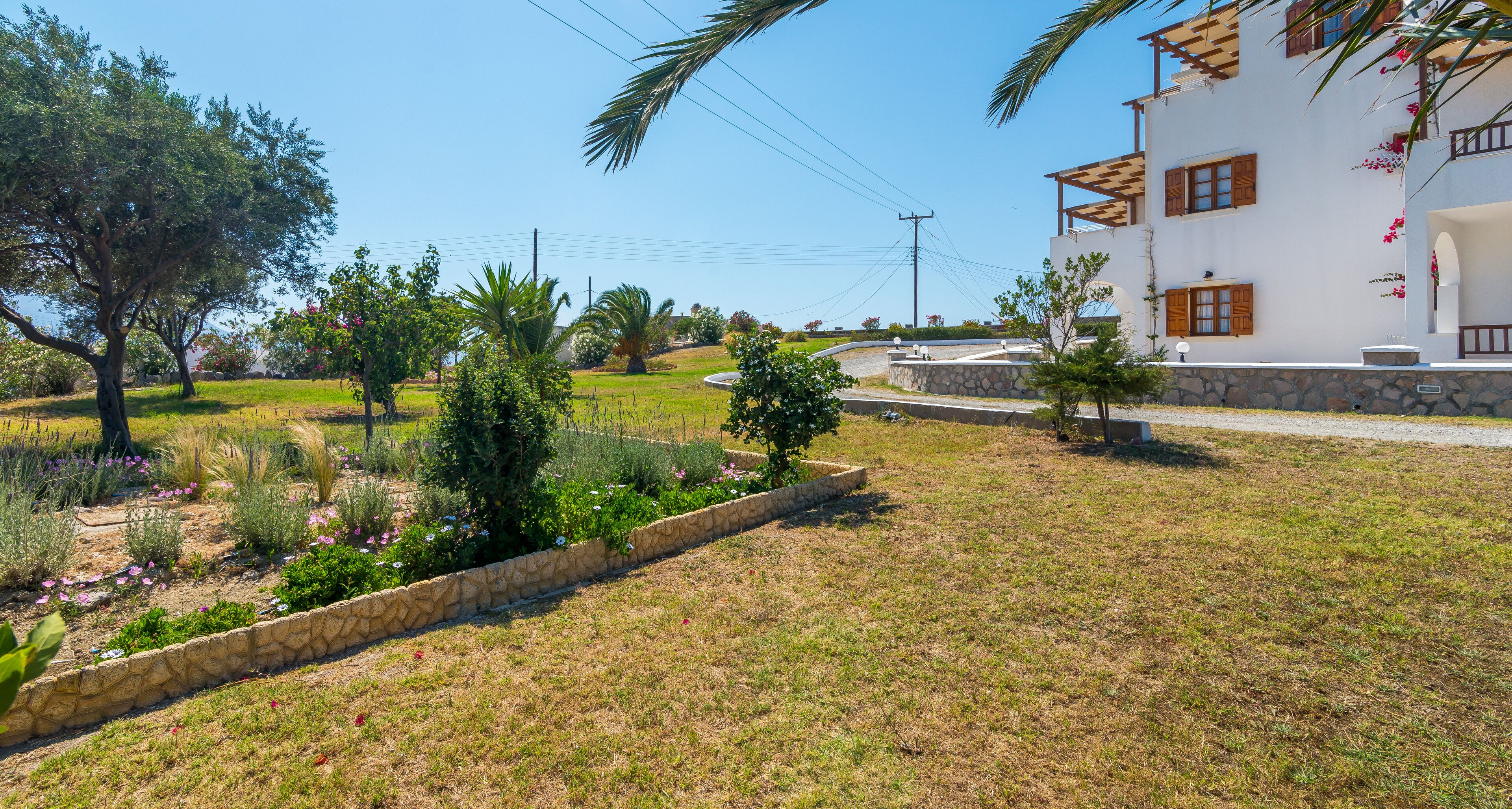 Um edifício branco com um caminho de pedra, rodeado por um jardim bem cuidado com diversas plantas e flores.