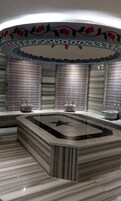 Uma área de spa com uma banheira de hidromassagem central, paredes revestidas com um padrão ondulado e um teto decorativo com motivos florais.