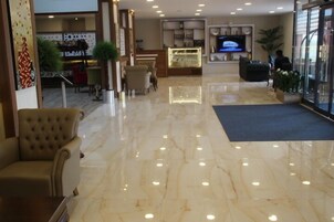 Um hall de hotel com piso de mármore, balcão de recepção, televisão e áreas de estar.