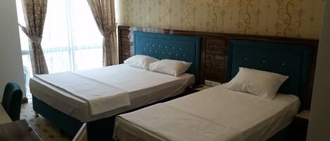 Duas camas de solteiro com cabeceiras, uma mesinha e uma cadeira num quarto de hotel com papel de parede estampado e um candelabro.