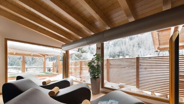 Uma área de spa com cadeiras de massagem, uma janela grande com vista para uma paisagem nevada e vigas de madeira no teto.
