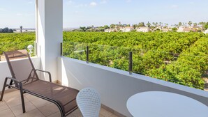 Uma varanda com vista para um vinhedo, uma cadeira branca, uma cadeira de metal e uma pequena mesa.