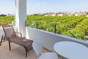 Uma varanda com vista para um vinhedo, uma cadeira branca, uma cadeira de metal e uma pequena mesa.