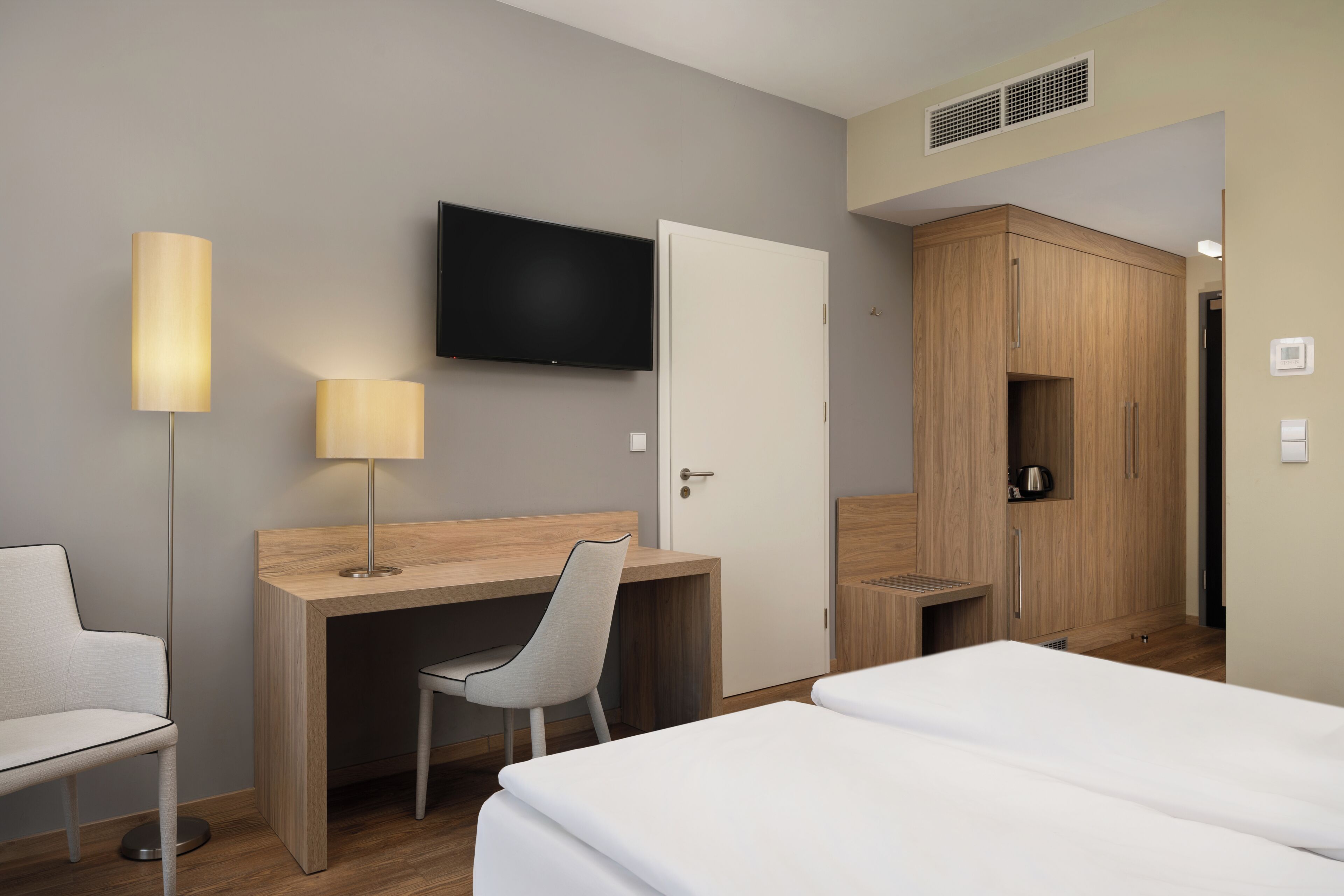 Quarto de hotel com cama, escrivaninha, cadeira, televisão e guarda-roupa.