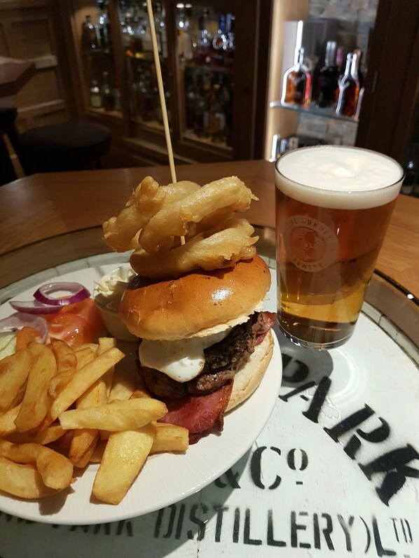 Uma refeição com hambúrguer, batatas fritas e uma cerveja em uma mesa, com uma placa que diz 'DISTILLERY'.