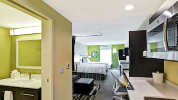 Quarto de hotel com banheiro, cama, escrivaninha e cozinha compacta.