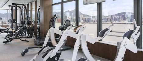 Uma academia com aparelhos de cardio, equipamentos de musculação e amplas janelas com vista para a cidade.