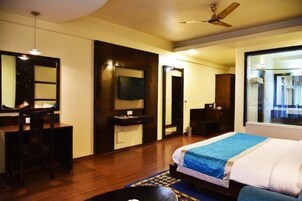 Quarto de hotel com cama, escrivaninha com cadeira, televisão e ventoinha no teto.