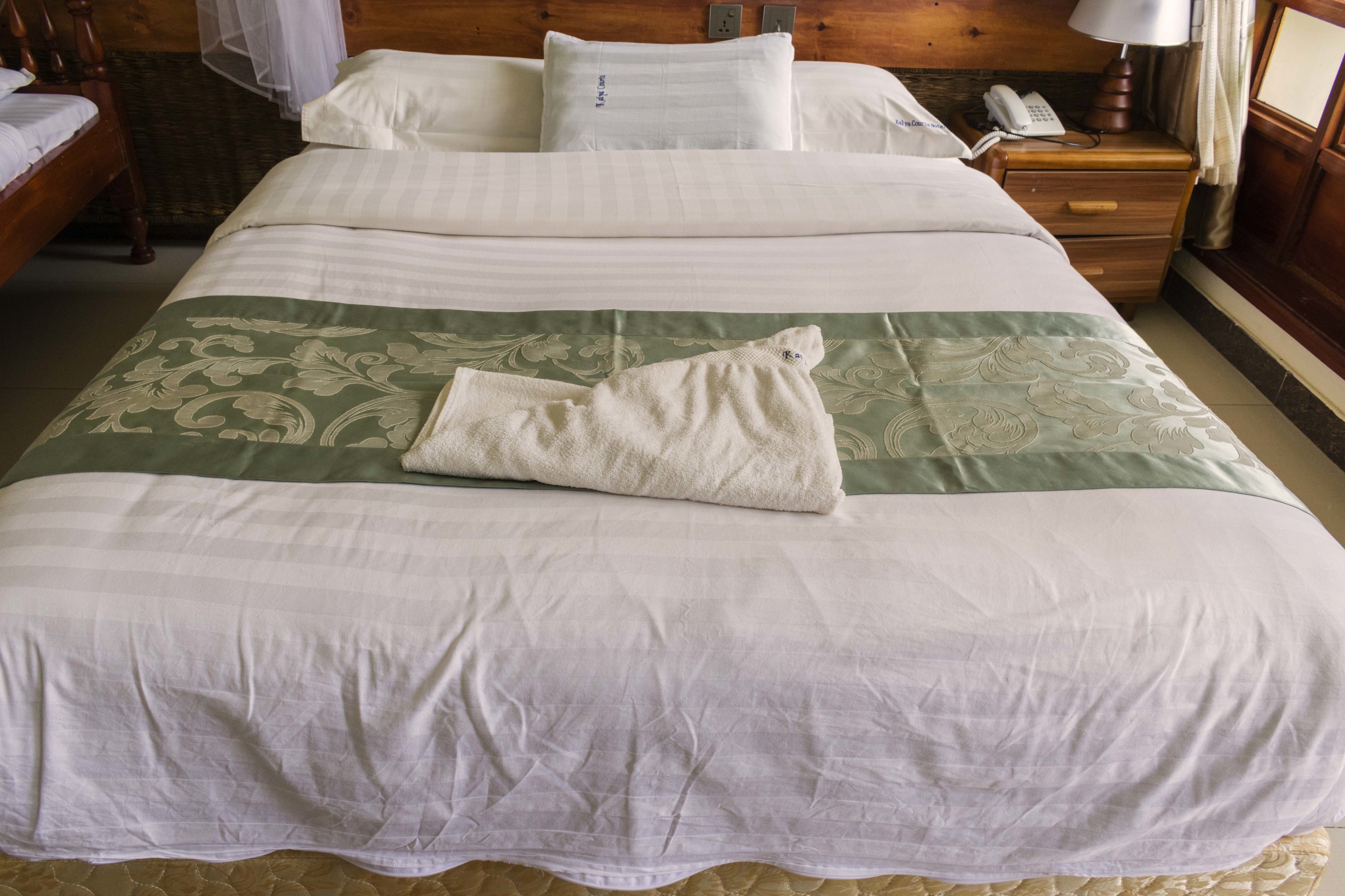 Uma cama bem arrumada com um edredom verde e branco, um travesseiro branco e uma toalha dobrada sobre a cama.