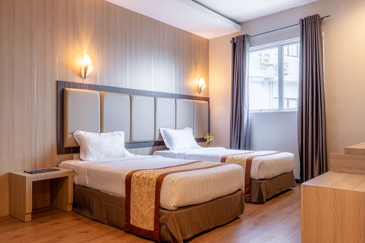 Quarto de hotel com duas camas, paredes de painel de madeira, uma janela com cortinas e uma mesa de cabeceira com abajur.