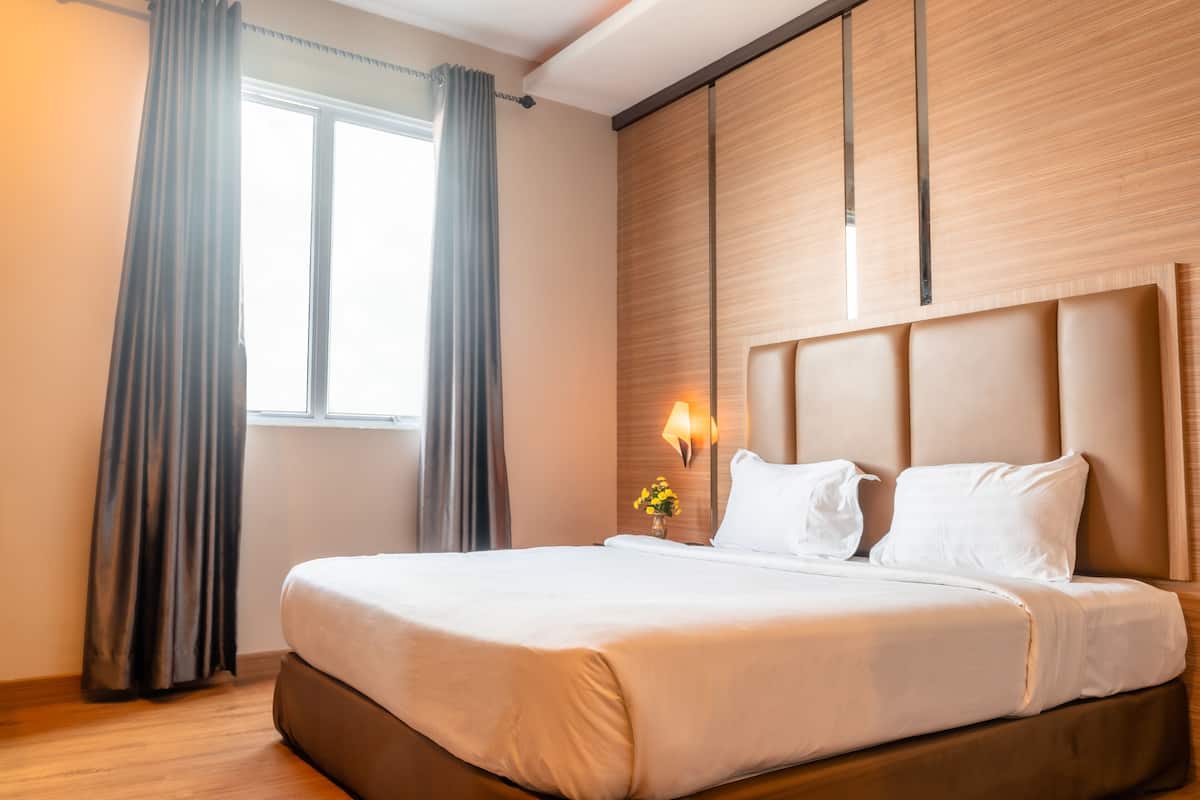 Cama bem arrumada com cabeceira, janela com cortinas e luminária fixada na parede.