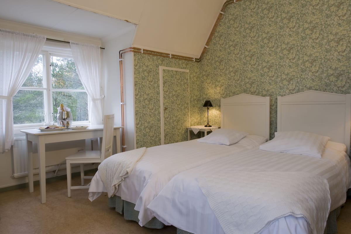 Quarto com cama grande, escrivaninha com cadeira, mesa de cabeceira e janela com cortinas.