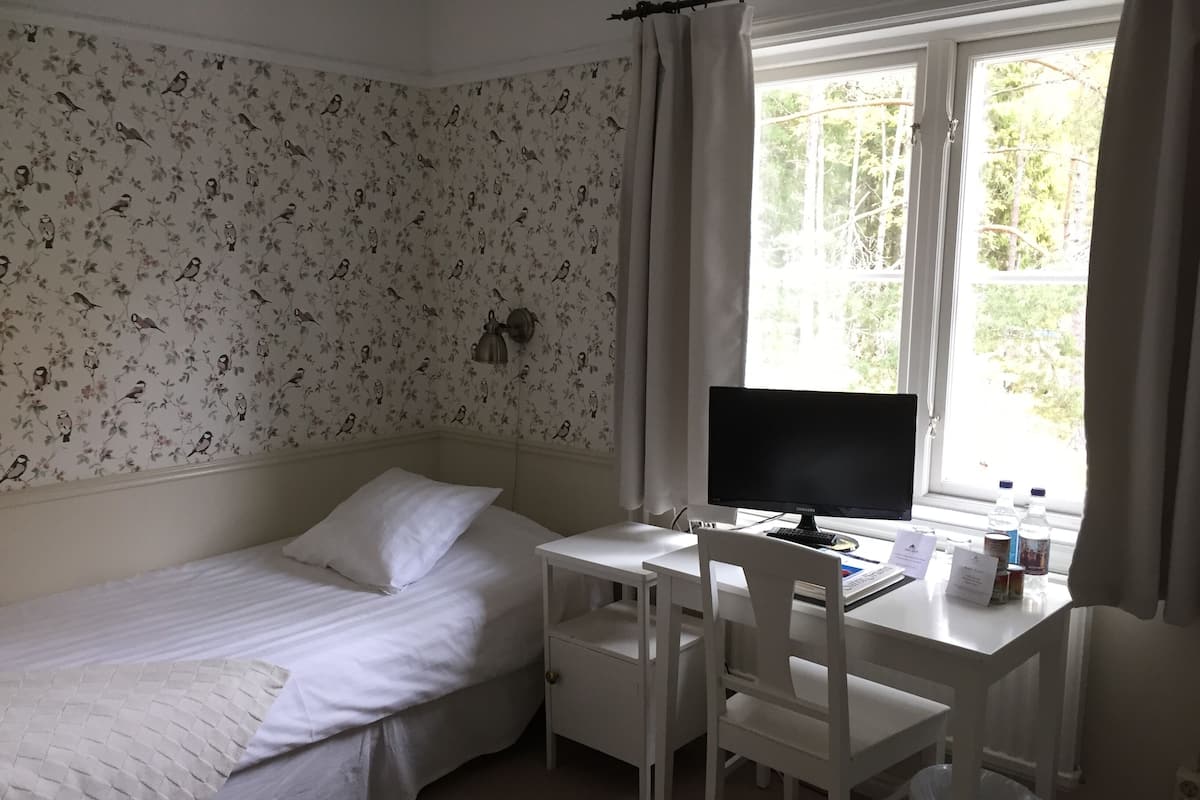 Quarto com cama, escrivaninha com computador e janela com cortinas.