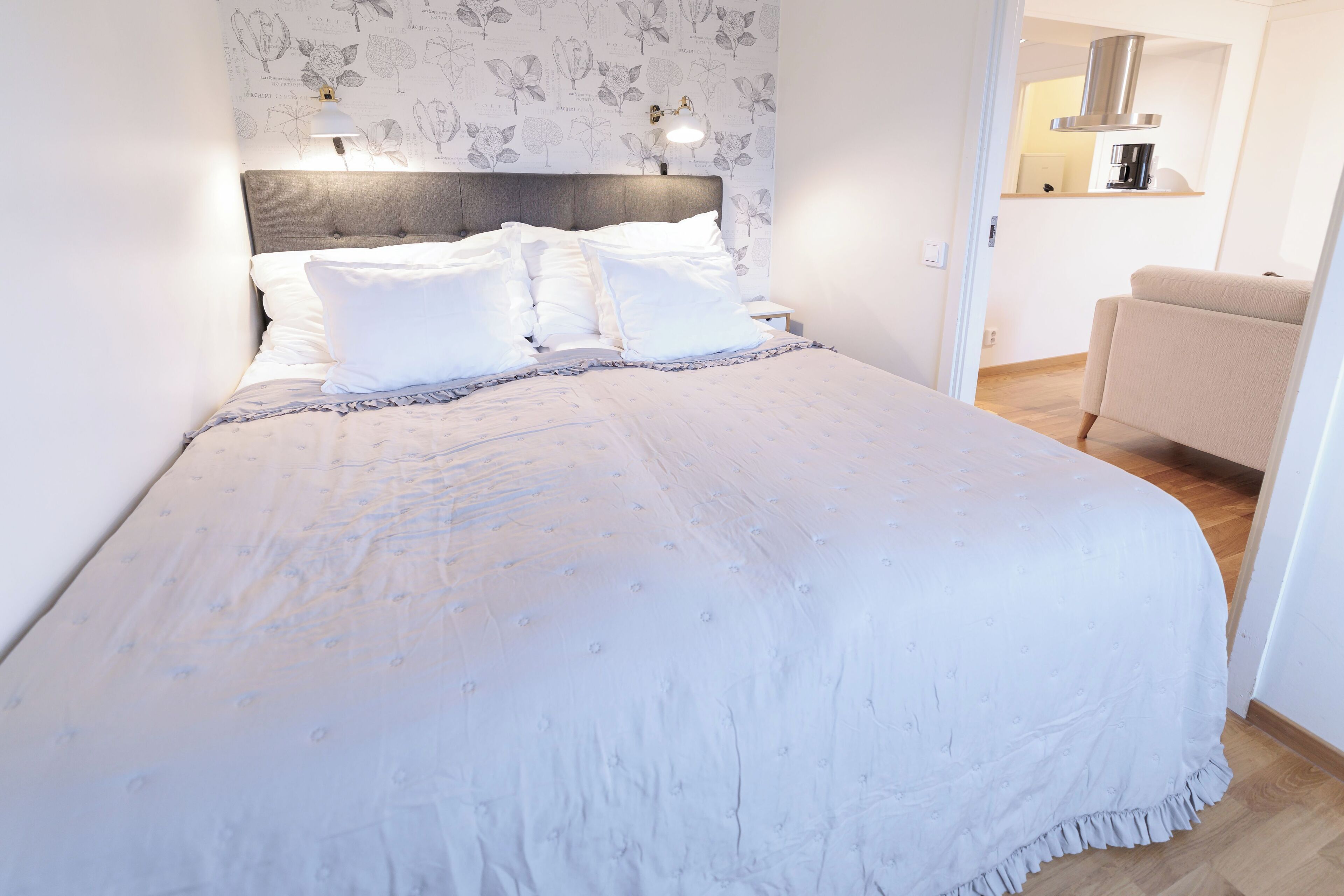 Cama bem arrumada com colcha estampada e almofadas, cabeceira e abajur.