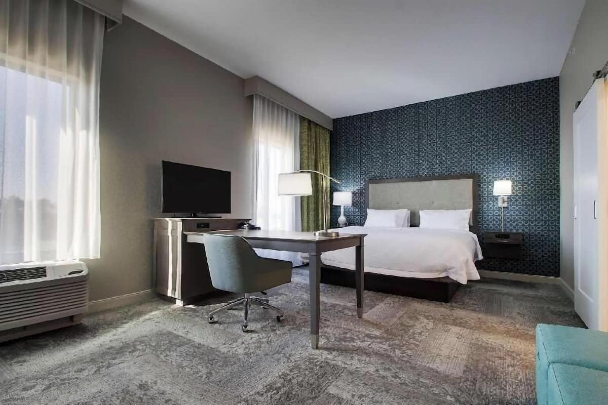 Quarto de hotel com cama, escrivaninha, cadeira, televisão e ar condicionado.