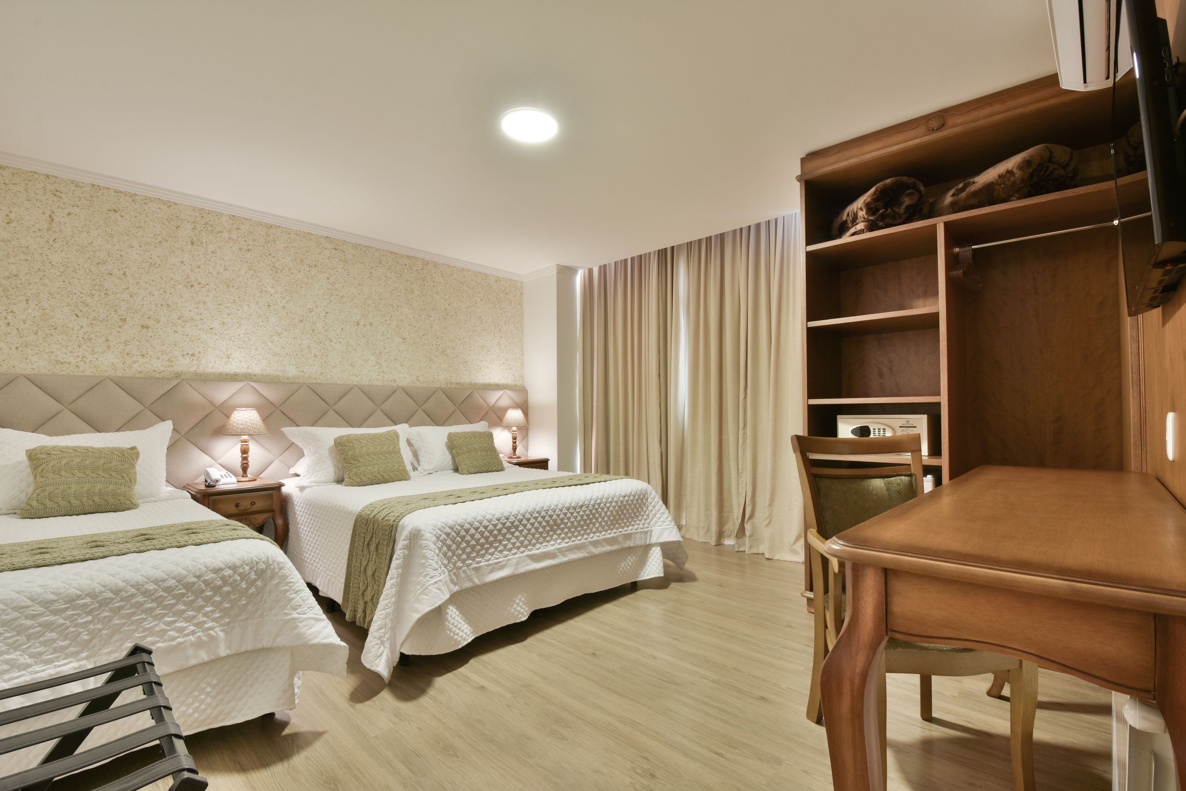 Quarto de hotel com duas camas, uma escrivaninha de madeira, uma cadeira, um guarda-roupa e uma mesa de cabeceira com luminárias.