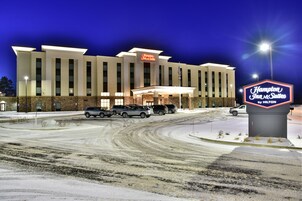 Um Hampton Inn & Suites by Hilton com um amplo estacionamento e neve no chão.