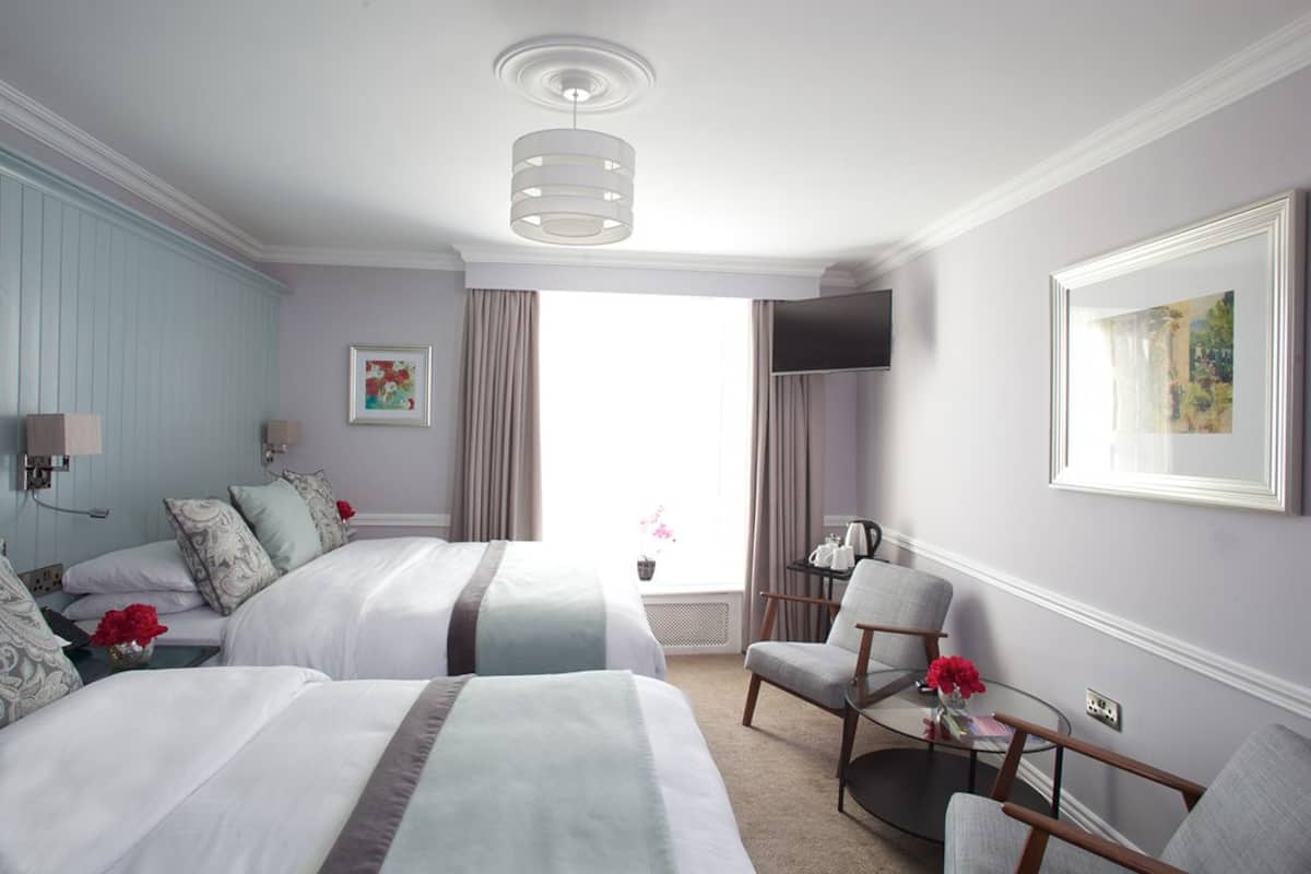 Quarto de hotel com duas camas, televisão, uma cadeira e uma mesa pequena com um vaso de flores.