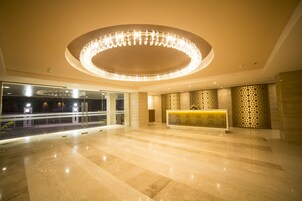 Um hall amplo com um lustre circular, uma mesa de recepção e uma parede com padrão.