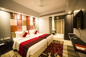 Quarto de hotel com uma cama grande, uma escrivaninha, um espelho e uma televisão.