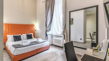 Quarto de hotel com cama, poltrona, escrivaninha, espelho e janela com cortinas.