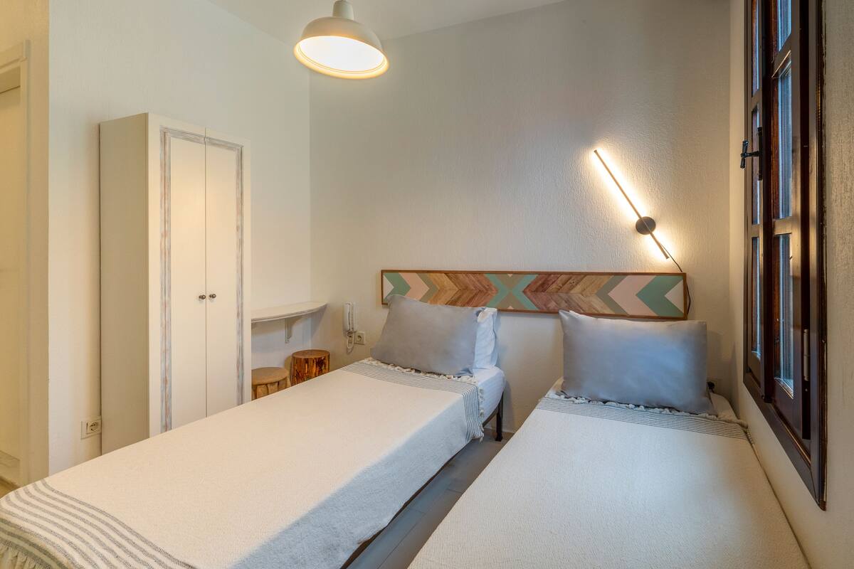 Quarto com duas camas, cabeceira de madeira, mesa de cabeceira e janela com vista.