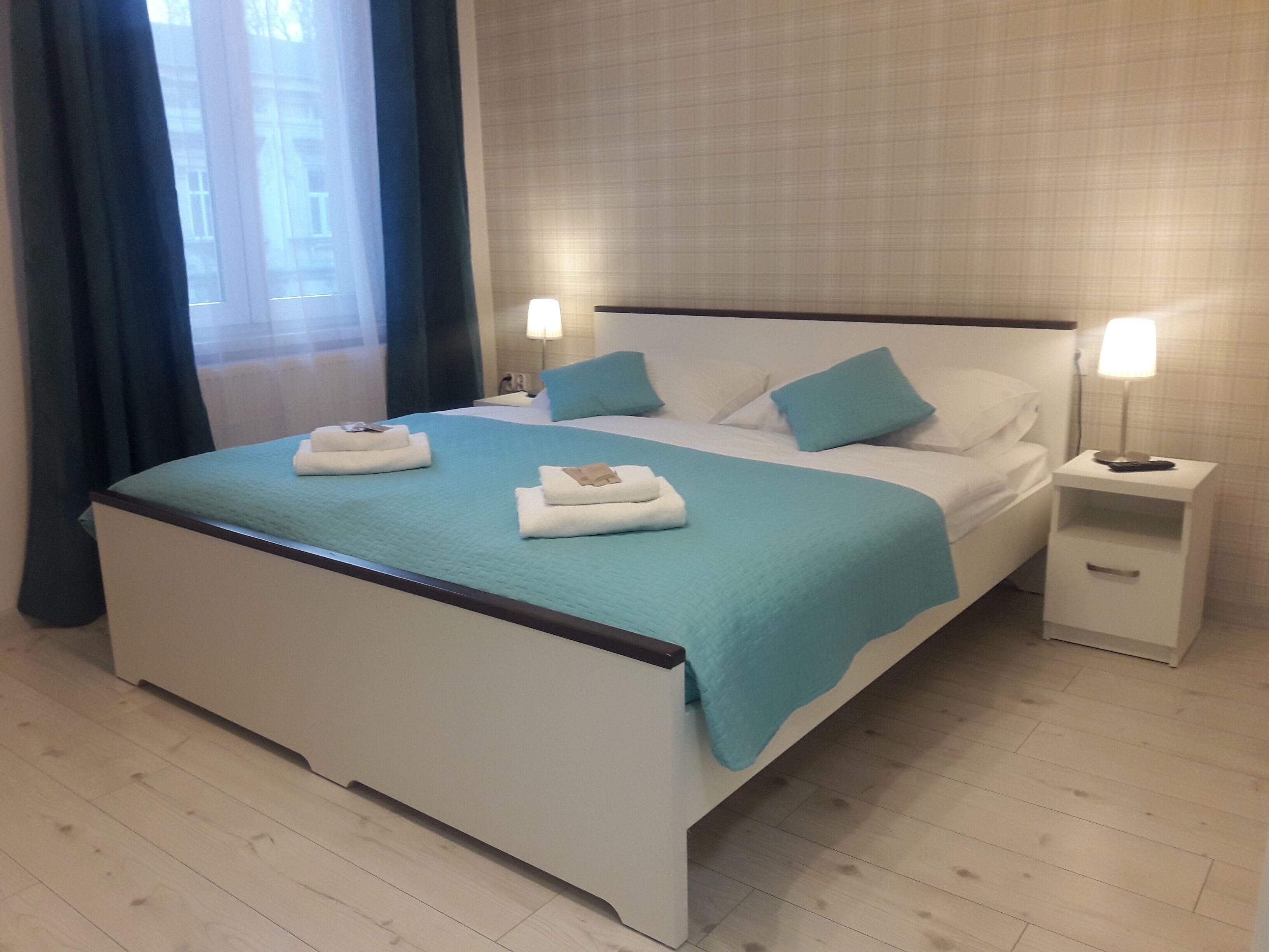Quarto de hotel moderno com uma cama grande, duas mesas de cabeceira e vista para a cidade pela janela.