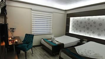 Quarto de hotel com duas camas, uma escrivaninha com cadeira, um radiador e uma janela com persianas.