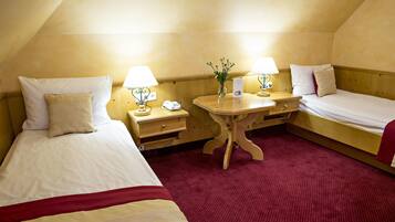 Quarto de hotel com duas camas de solteiro, uma mesa de cabeceira de madeira com abajur, uma pequena mesa com um vaso e um tapete vermelho.