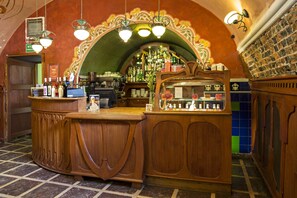 Uma área de bar com balcão de madeira, caixa registradora e variedade de garrafas expostas.