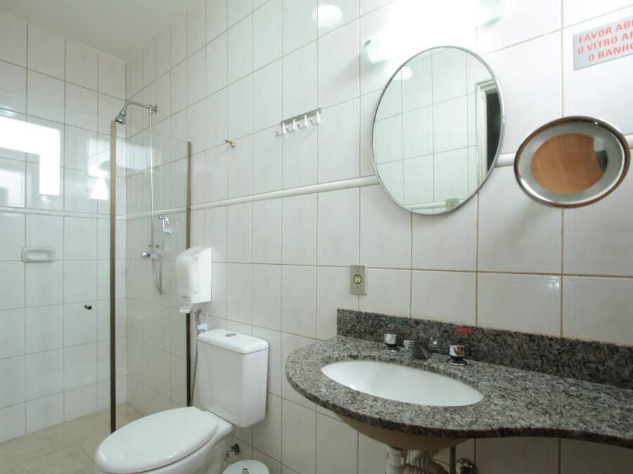 Casa de banho com sanita, chuveiro, lavatório e dois espelhos.
