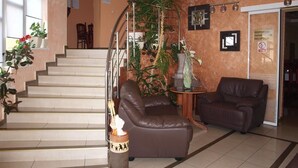 Um saguão com uma escadaria, uma mesa de recepção, um sofá de couro marrom e um vaso de planta.
